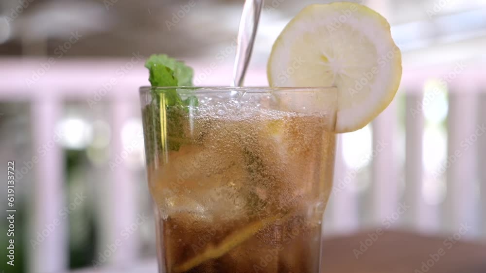 Close-up pouring sparkling water into syrup into glass with slice lemon and ice cubes. Fresh ...