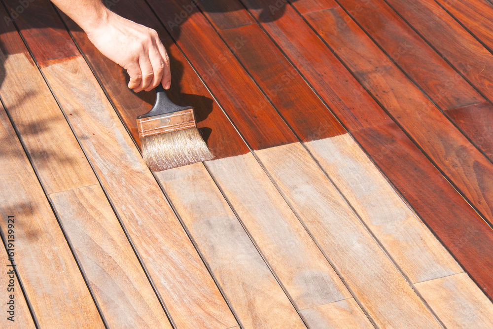 Ipe wood worker's hand is oiling terrace decking with a painting brush ...