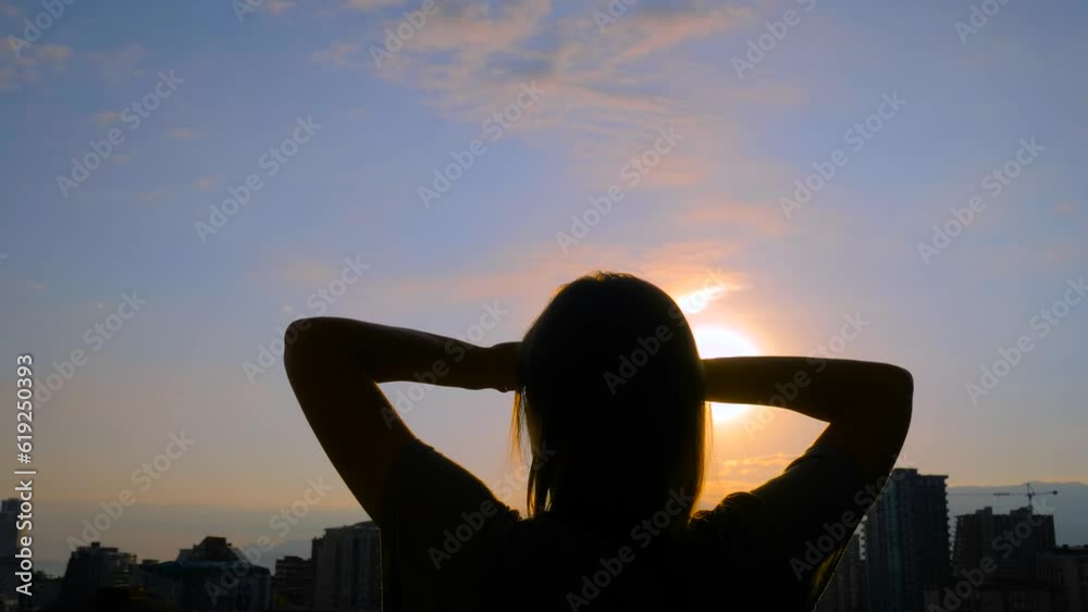 Back view: woman silhouette is stretching arms up against the sunrise ...