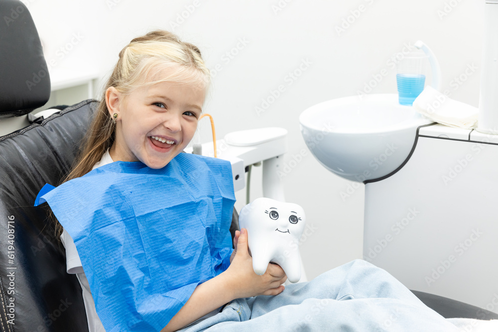 Happy little child sits in a dental chair and shows an artificial model ...