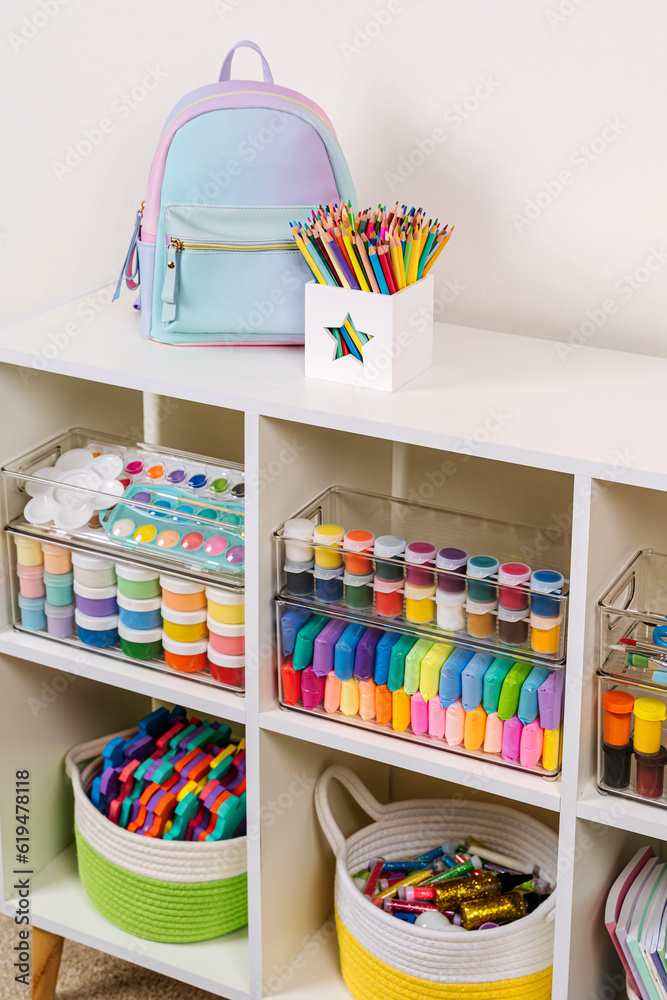 White shelving with kids backpack and various material for creativity ...