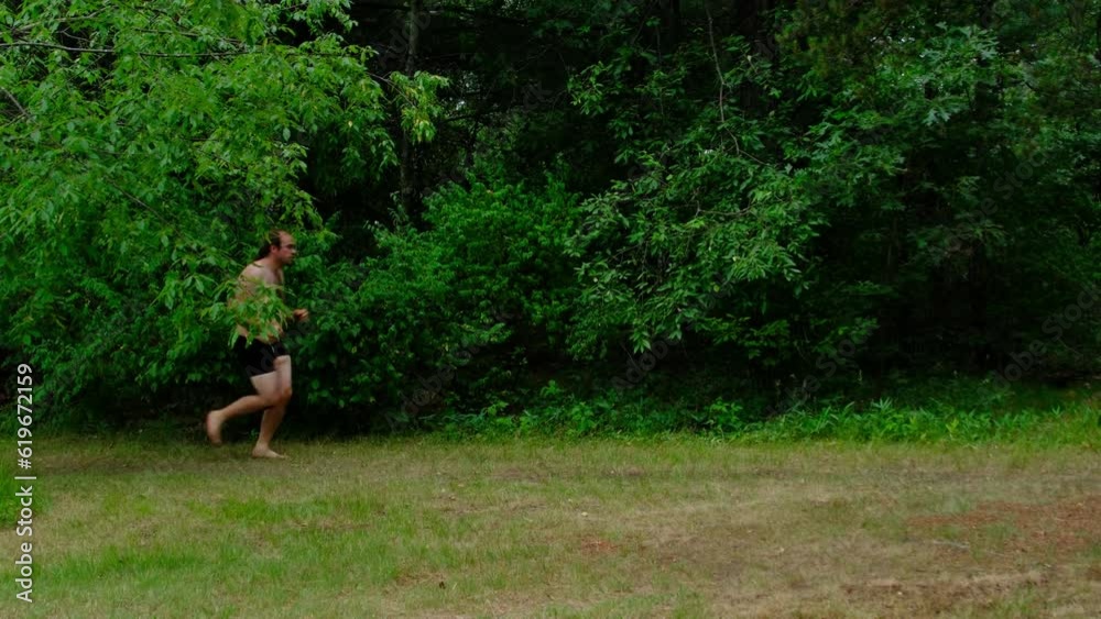 Slow motion of shirtless fat man running left to right against woods ...