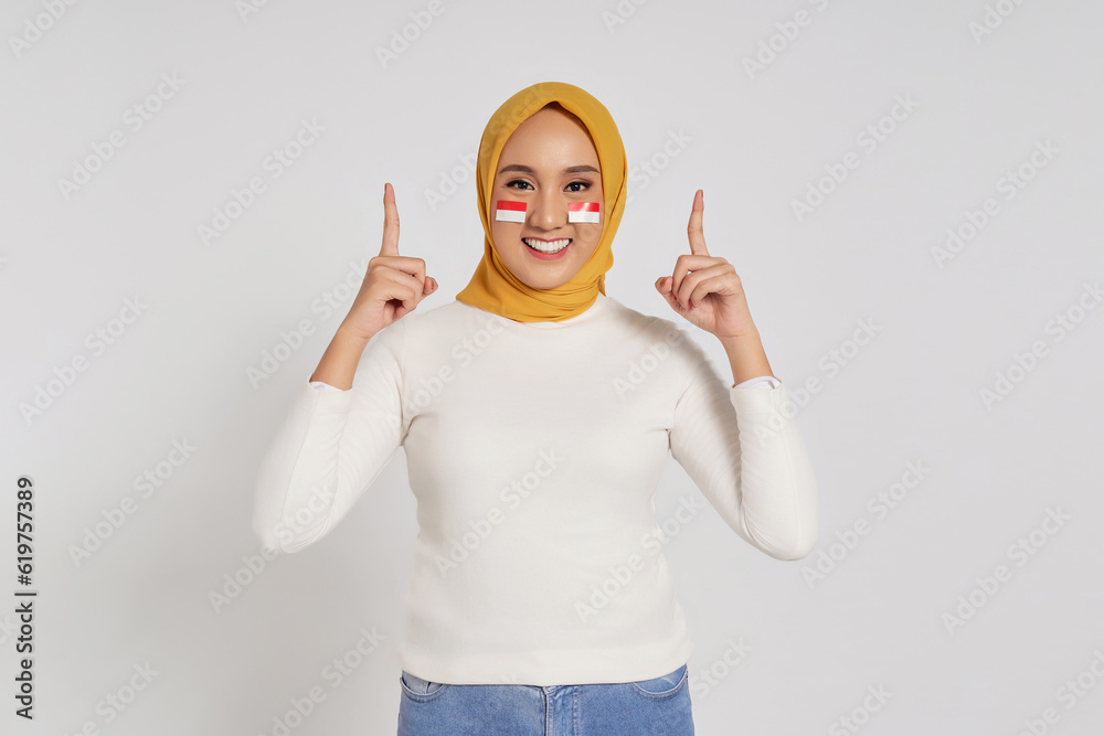 Smiling young Asian Muslim woman wearing hijab pointing her finger up ...