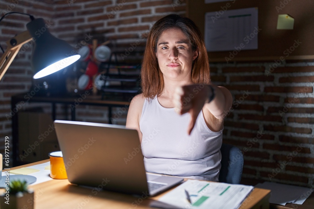 Brunette woman working at the office at night looking unhappy and angry ...