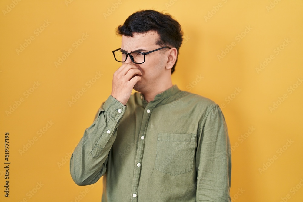 Non binary person standing over yellow background smelling something ...