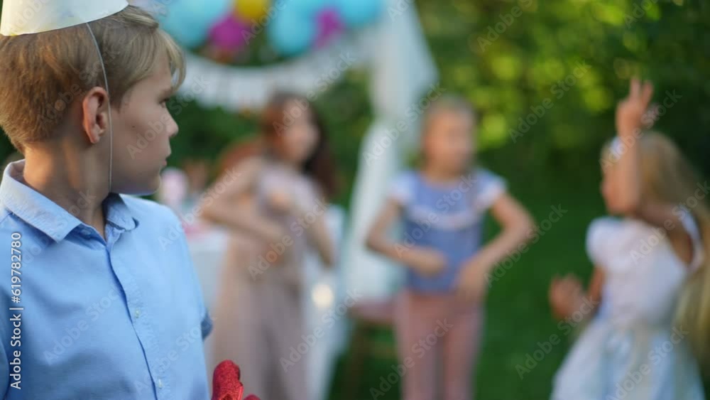Bored sad Caucasian birthday boy looking back at blurred cheerful girls ...