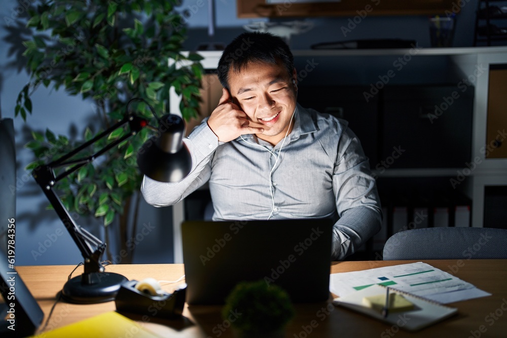 Young chinese man working using computer laptop at night smiling doing ...