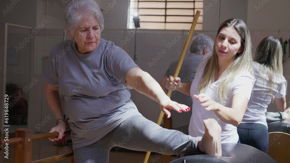 Female Pilates coach guiding a senior woman to stretch leg in ...