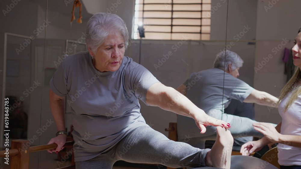Female Pilates coach guiding a senior woman to stretch leg in ...