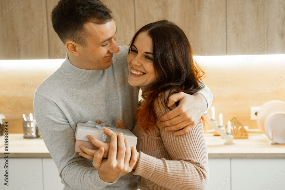 Loving couple at home. The man gives a gift. The woman laughs happily ...