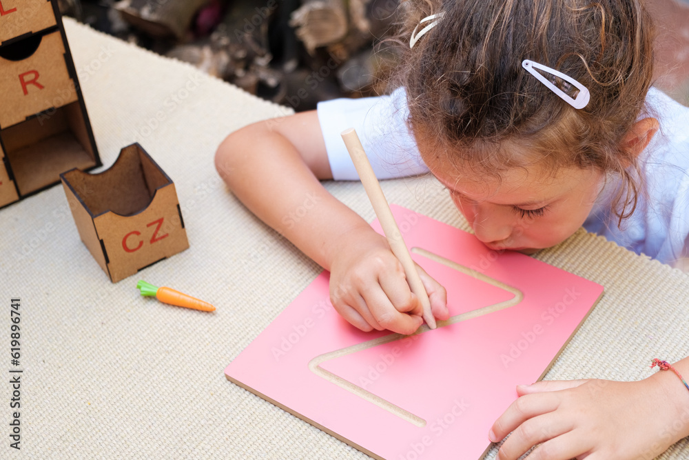 A girl tracing the outline of a letter, using the montessori ...