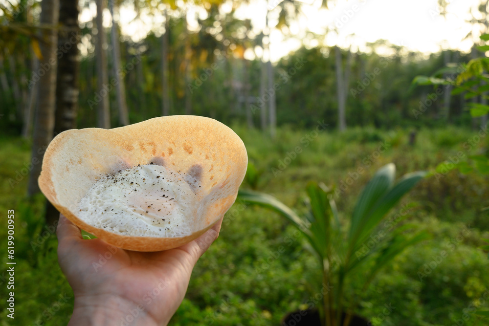 Sri lankan street food egg hopper in woman's hand for breakfast. Close ...