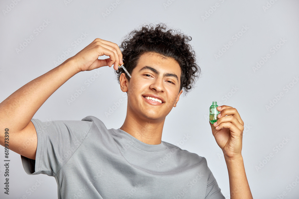 Young guy with black curly hair moisturizing his skin with a facial oil ...