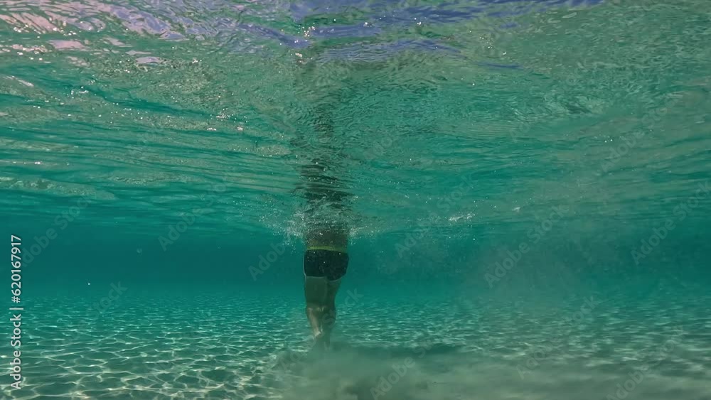 Underwater back view in shallow water of man walking on seabed raising ...