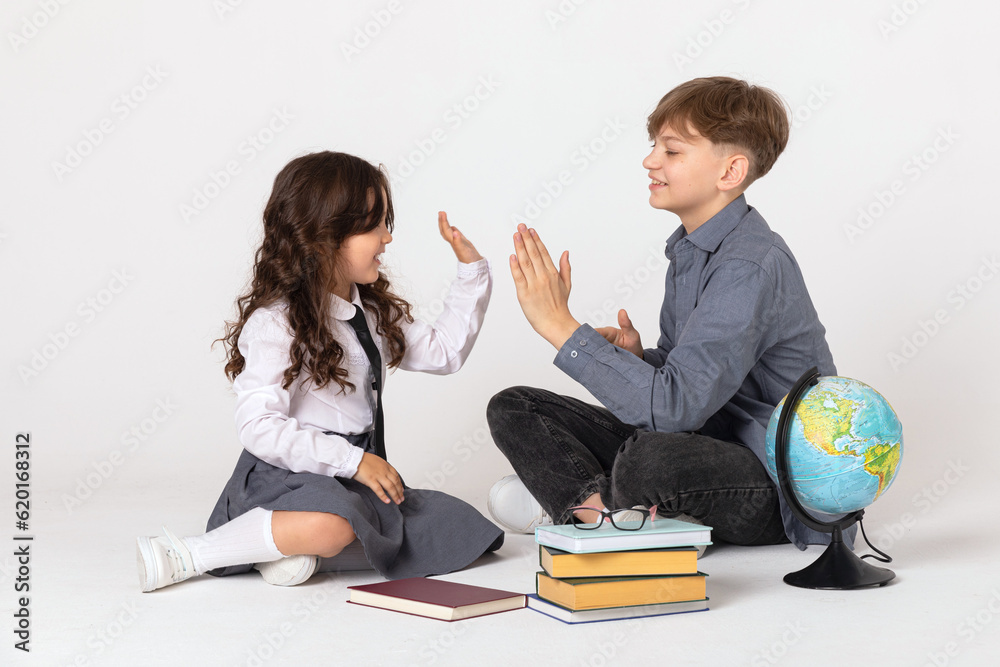 School children, a boy and a girl, sit opposite each other and clap ...