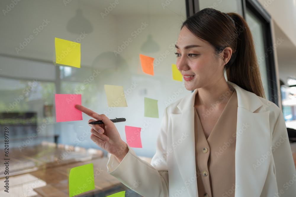 Asian businesswomen use post-it notes on glass walls to write strategic ...