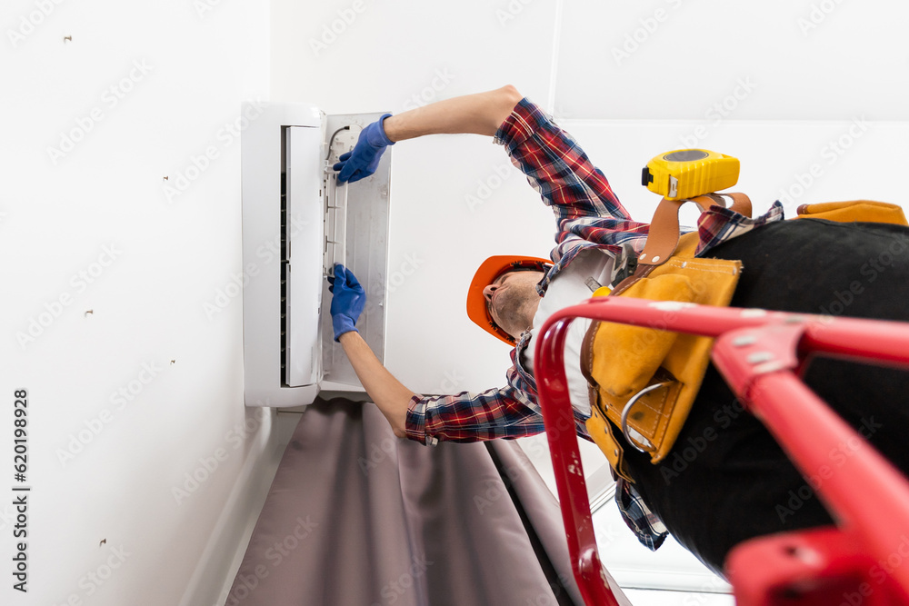Worker installing or repairing air conditioner. Young man in uniform ...