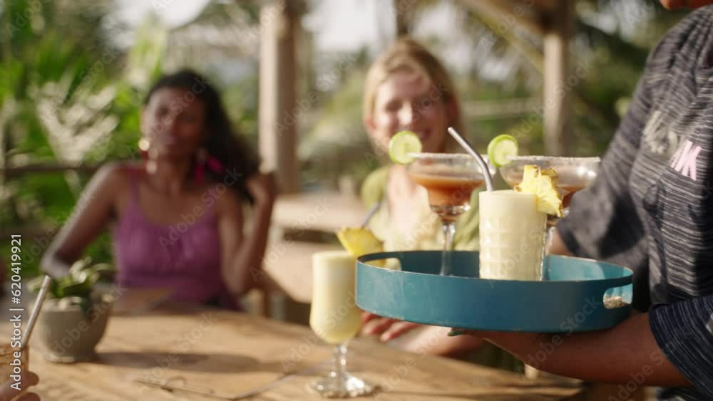 Woman waiter with tray serves cocktails to multiracial women in outdoor ...