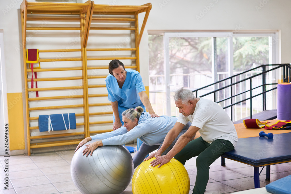 Physiotherapist guiding elderly patient exercising with fitness ball ...