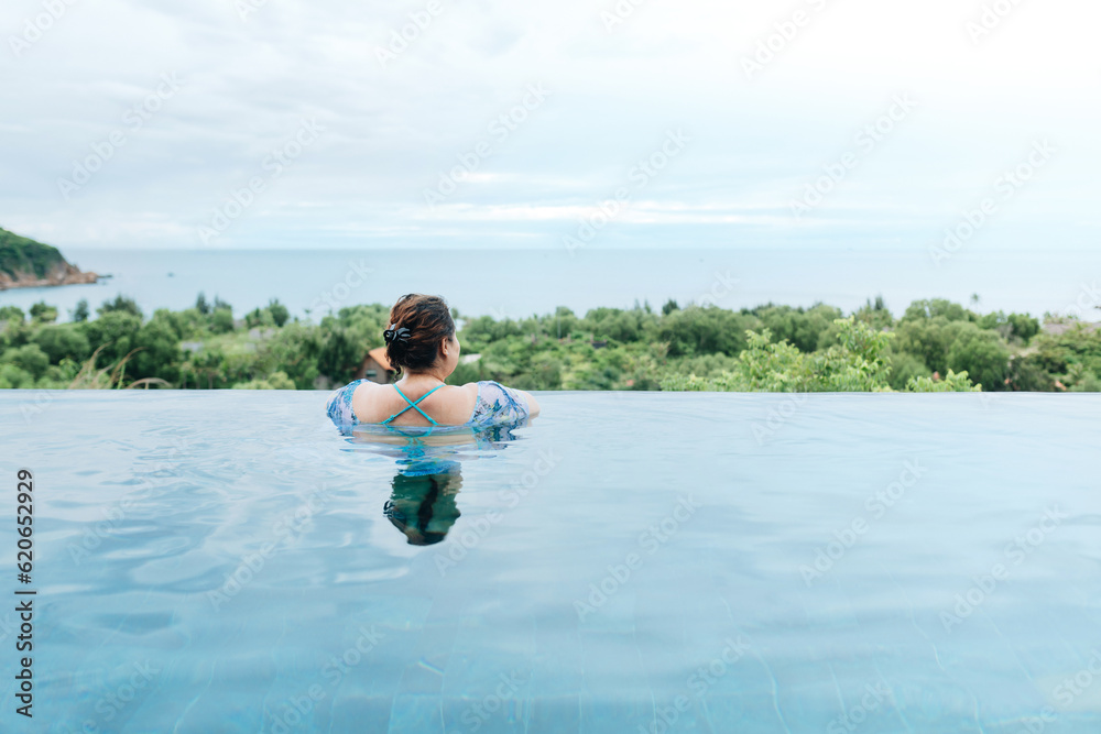 Foto de Back view of a woman in bikini having fun in infinity pool do ...
