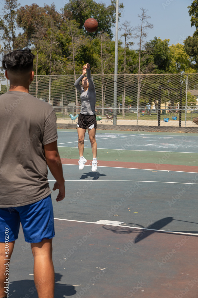 Latinx teen shooting hoop at basketball court while friends watches ...