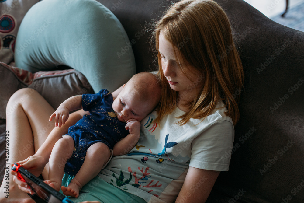 Tween Girl holding baby and playing video games Stock Photo | Adobe Stock