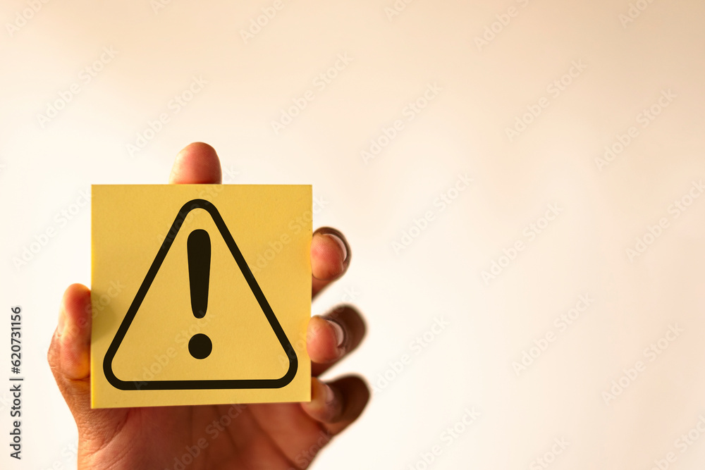 Hand holding yellow page with Exclamation mark or Warning sign over ...
