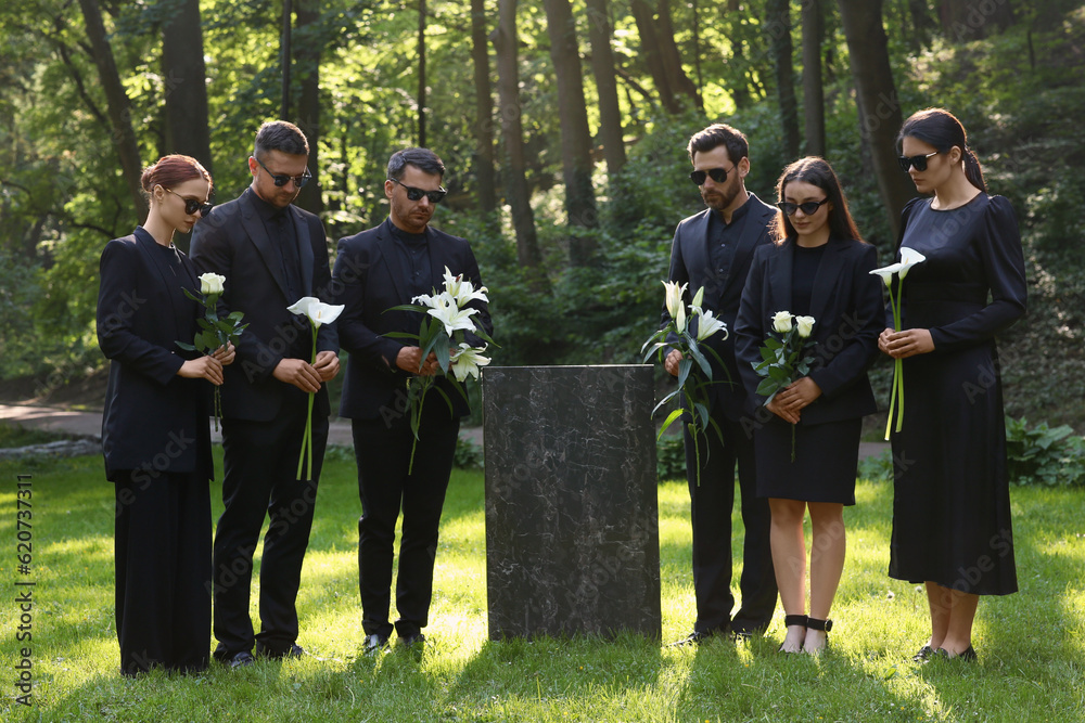 Sad people with flowers mourning near granite tombstone at cemetery ...