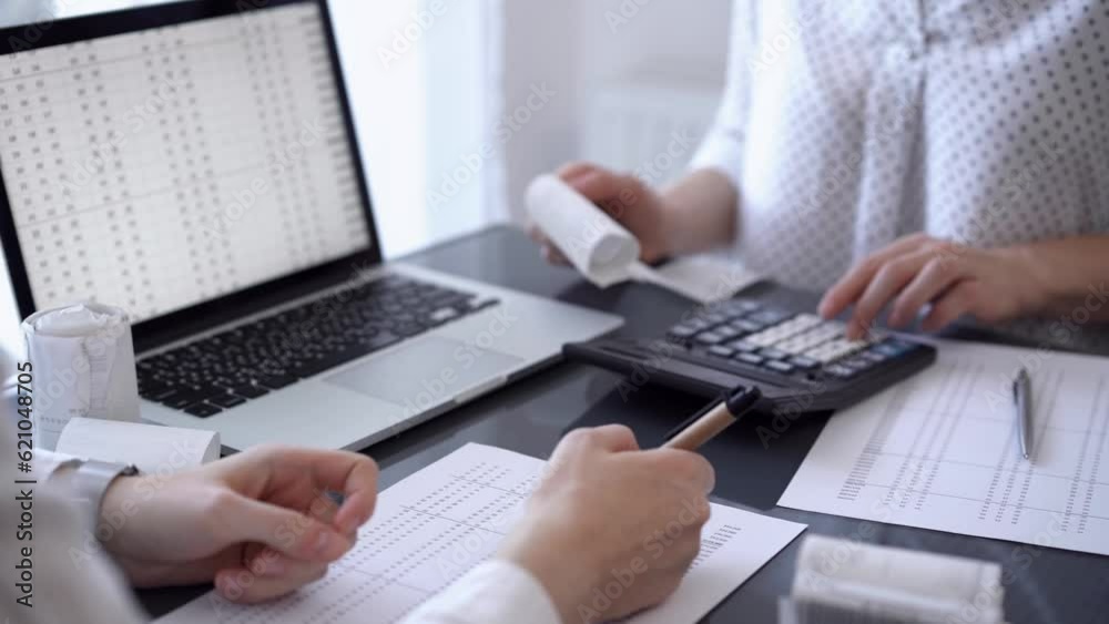 Two accountants use a calculator and laptop computer for counting taxes ...