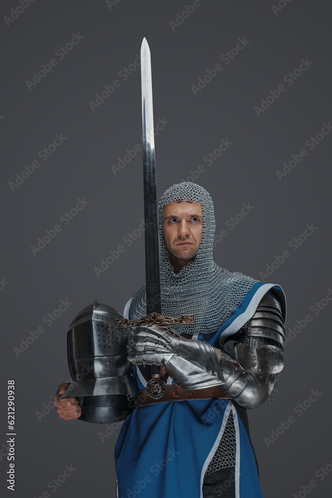 Proud knight stands holding his sword and helmet, donning blue surcoat ...