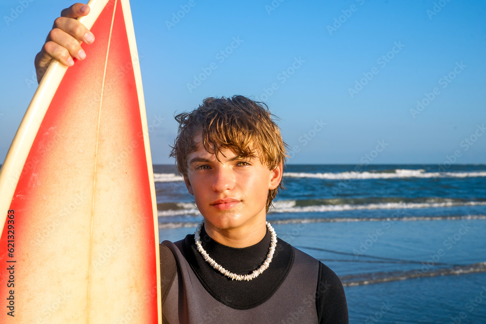 Teenage surfer boy standing on the beach while holding his surfboard ...