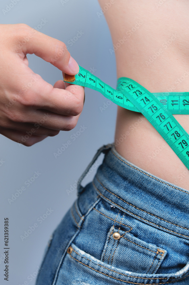 Waist of a slim woman in jeans. Close-up of a slim woman measuring the ...