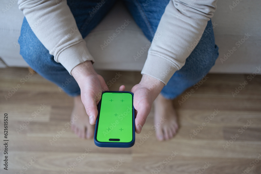 Man at home lying on a couch using smartphone with green mock-up screen ...