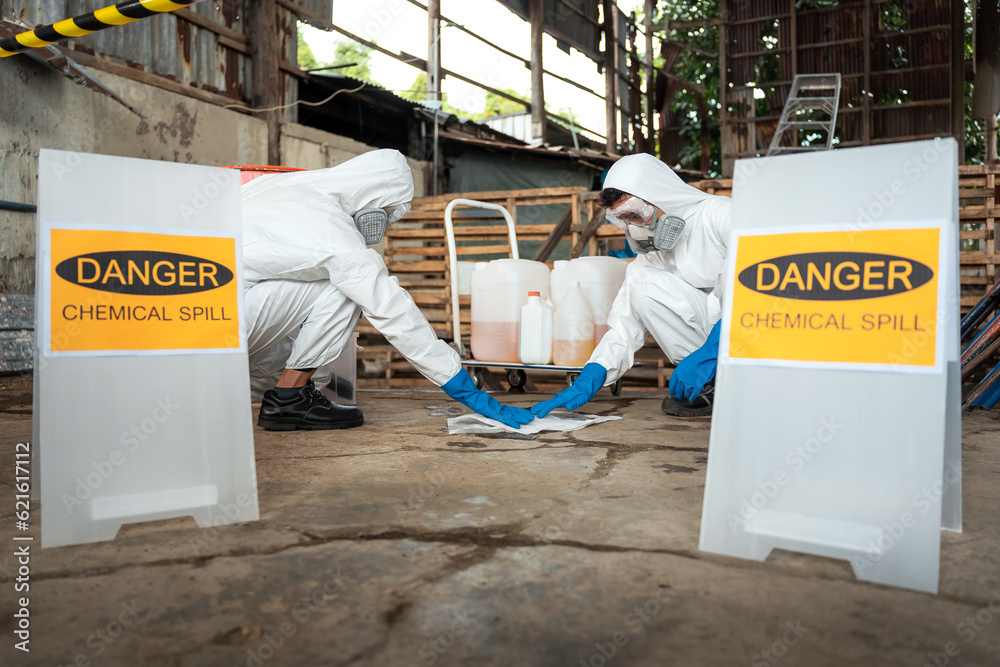 A team of two chemists, wearing PPE suits and gas masks, recover a ...