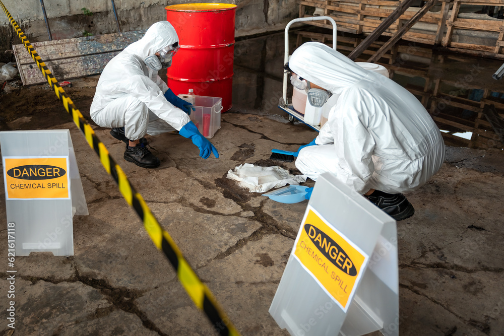 A team of two chemists, wearing PPE suits and gas masks, recover a ...