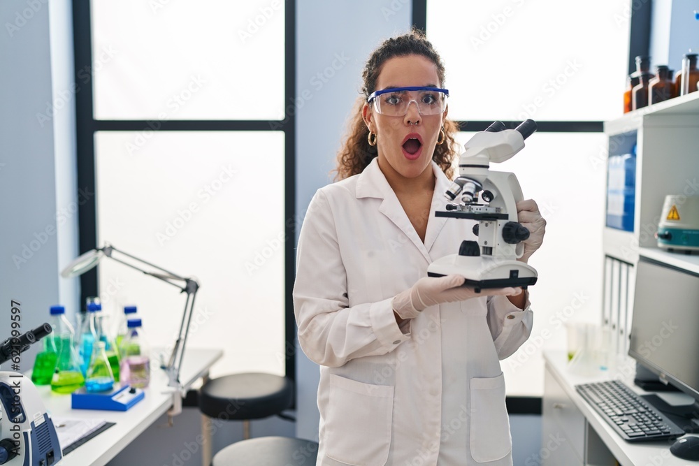 Young hispanic woman working at scientist laboratory afraid and shocked ...