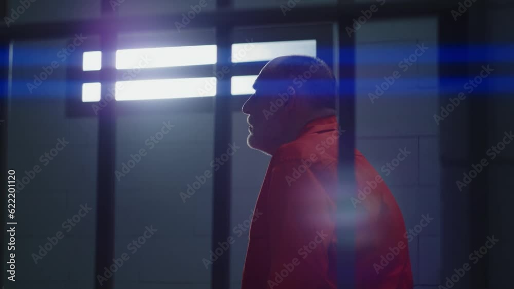 Elderly criminal in orange uniform sits in jail cell and looks on ...