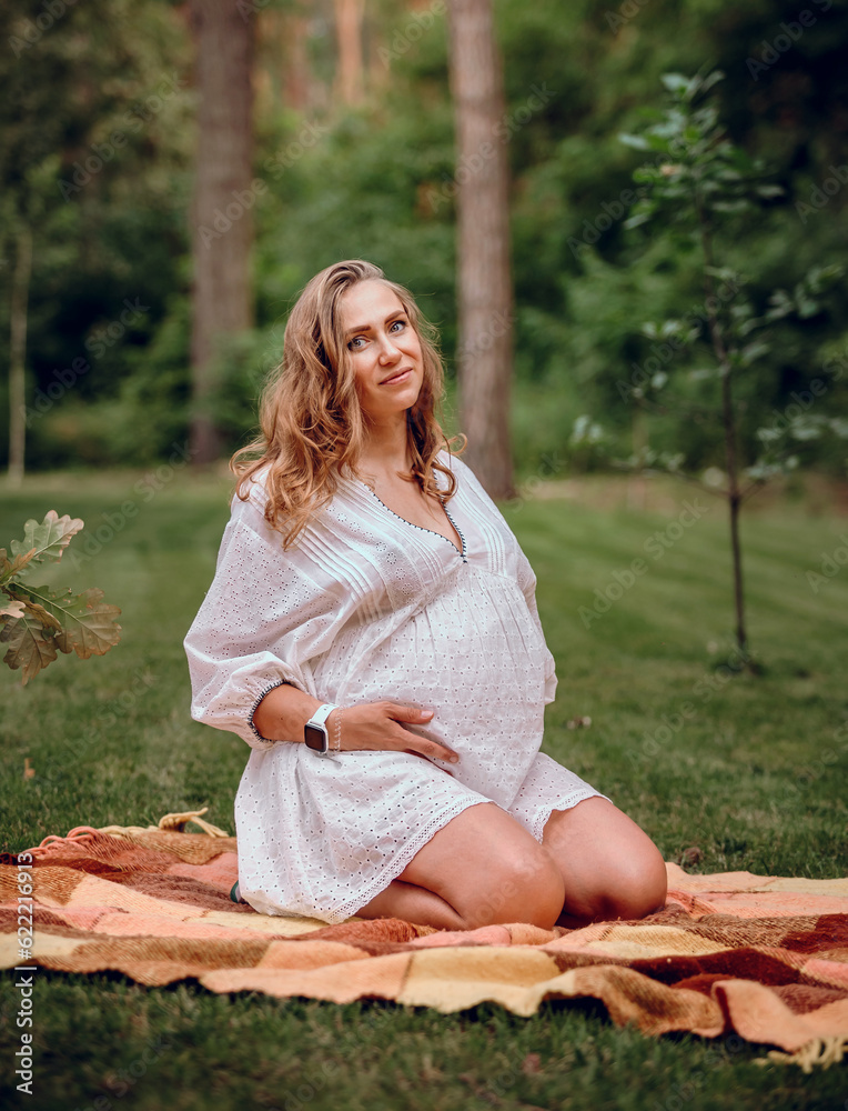 Pregnant woman in white boho summer dress sitting on the blanket with ...