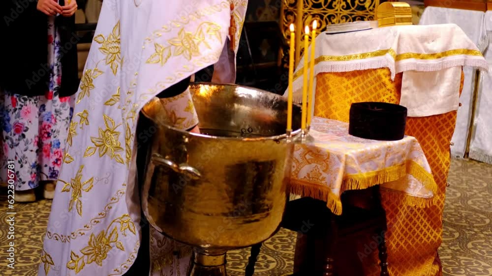 priest blesses water in a silver bowl for baptizing people in an ...