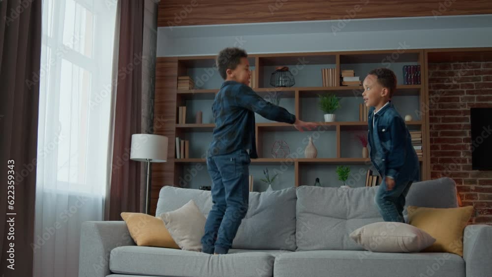 Two active naughty little boys children jumping on sofa at home African ...