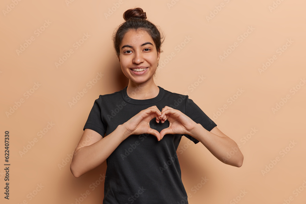 Iranian woman makes heart shape with her hands on abeige background ...