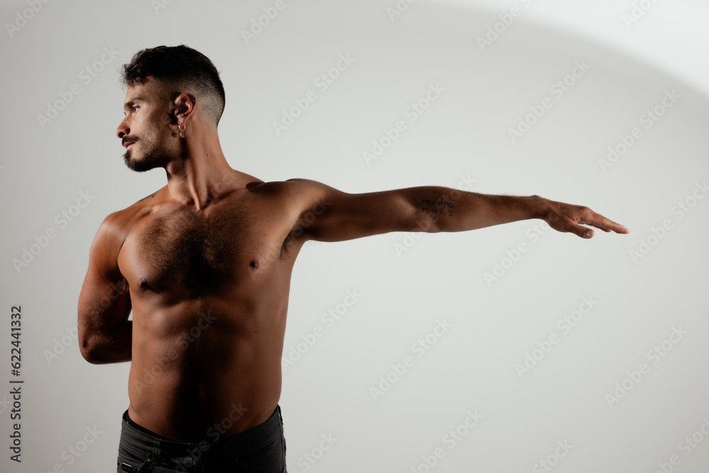 A shirtless man looks to the side, with one arm outstretched and the ...