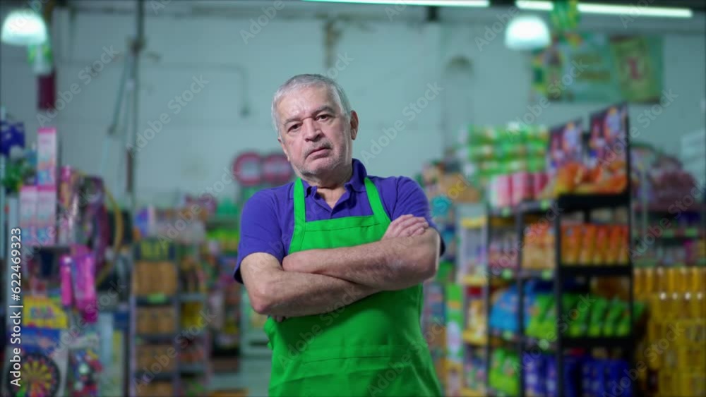 One serious older employee of grocery store crossing arms with stern ...