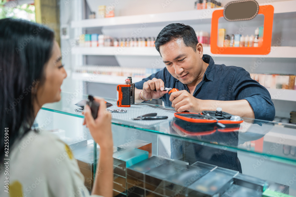 male vape shopkeeper changing the cotton coil while the female customer ...