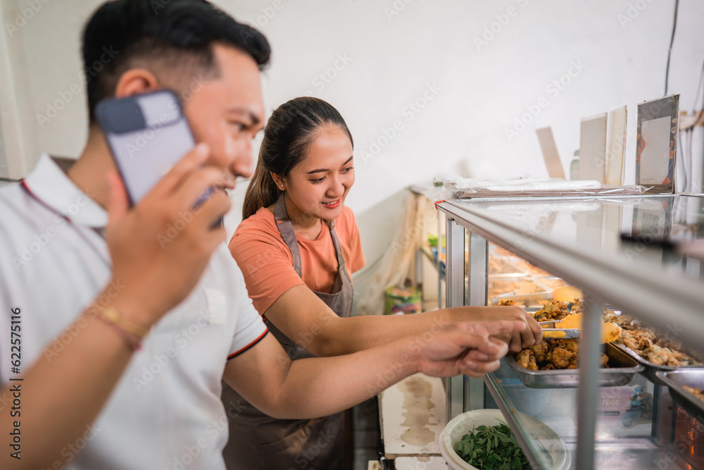 Asian female waiter helps male customer choose side dish using food ...