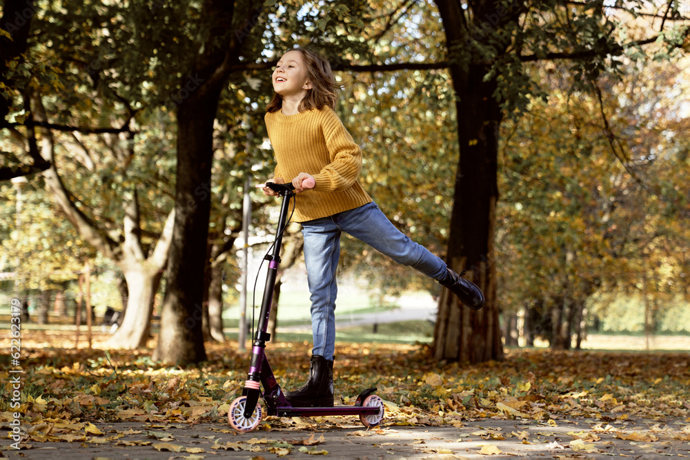 Caucasian child having fun in the woods while driving a push scooter ...