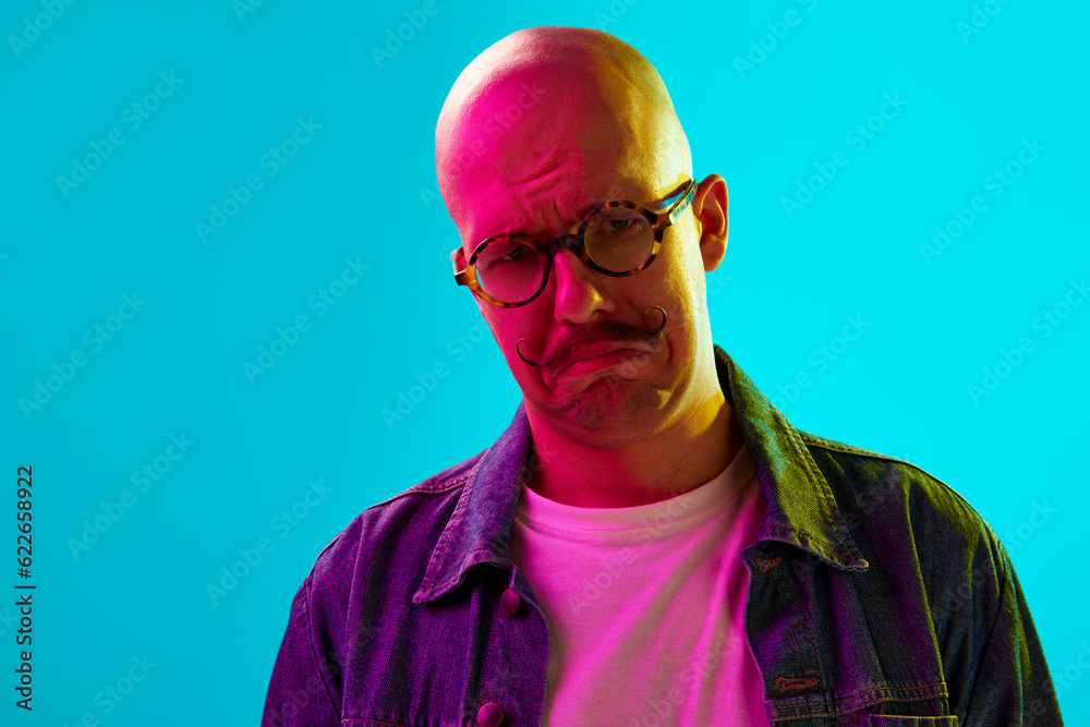 Portrait of young bald man with moustache against blue studio ...