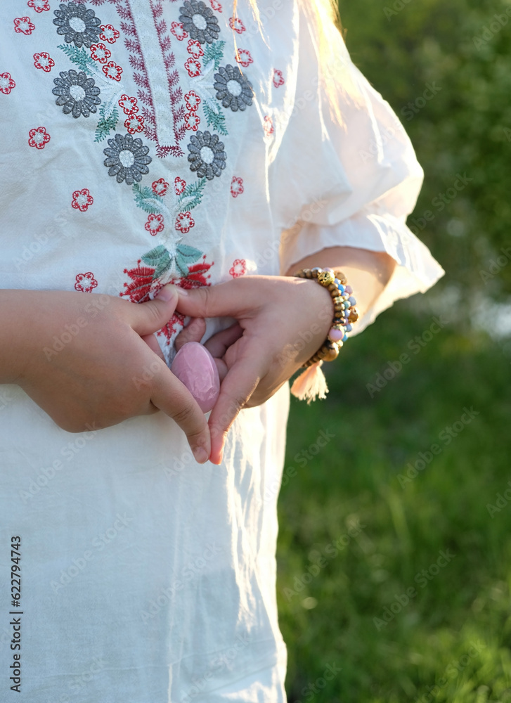 woman hands in Yoni mudra with rose quartz egg on white dress outdoor ...