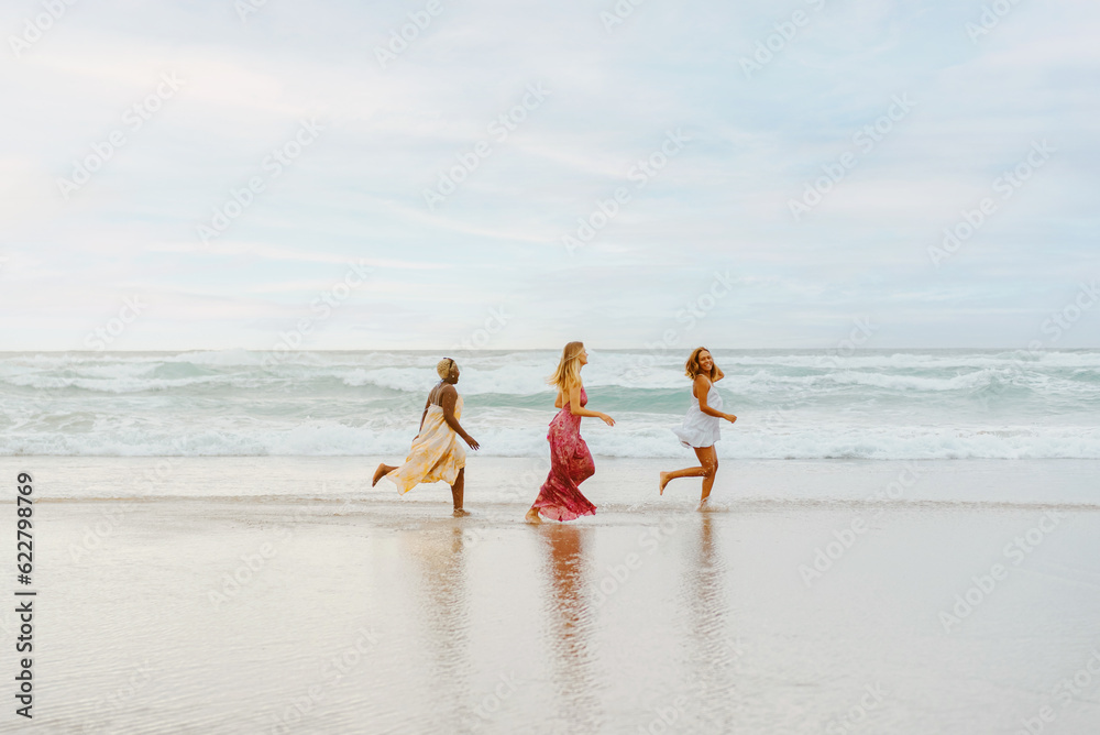 multiracial group of three young women running along the shore on the ...