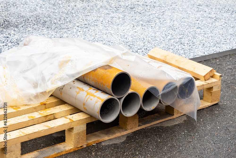 Old pipes are covered with foil. Pieces of rusty pipeline on pallets ...